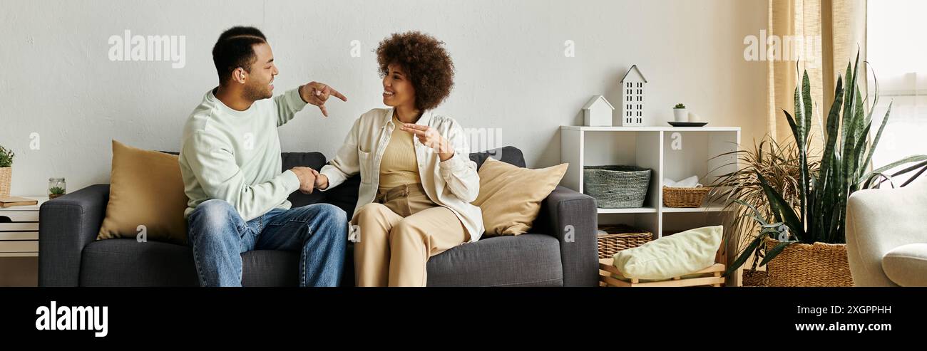 An African American couple sits on a couch, using sign language to ...