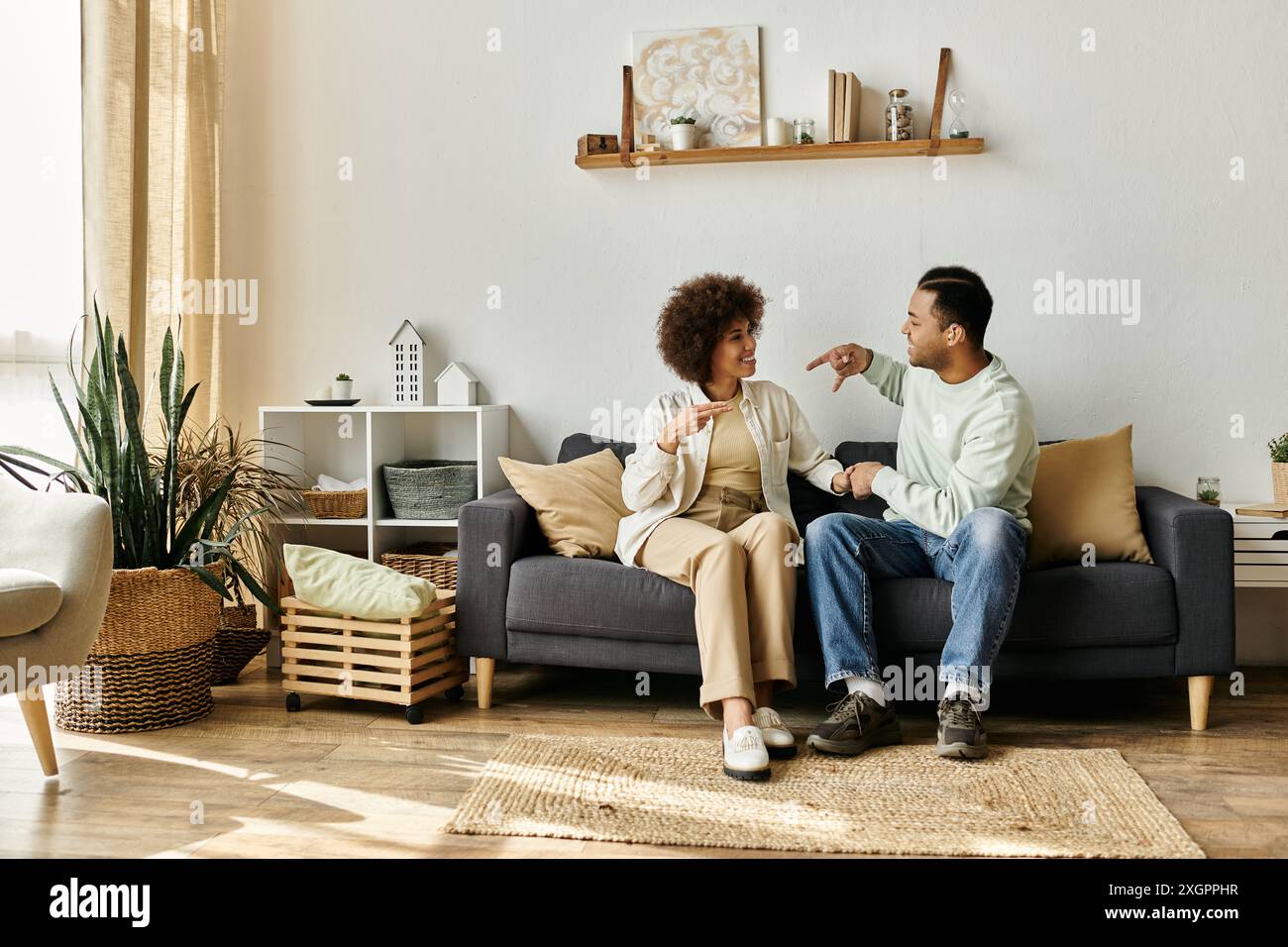 An African American couple sits on a couch at home and communicates ...