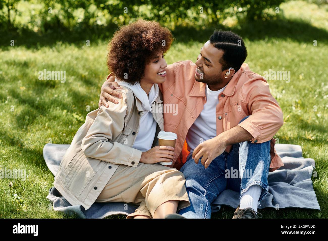 An African American couple sits on a blanket in a park, using sign ...