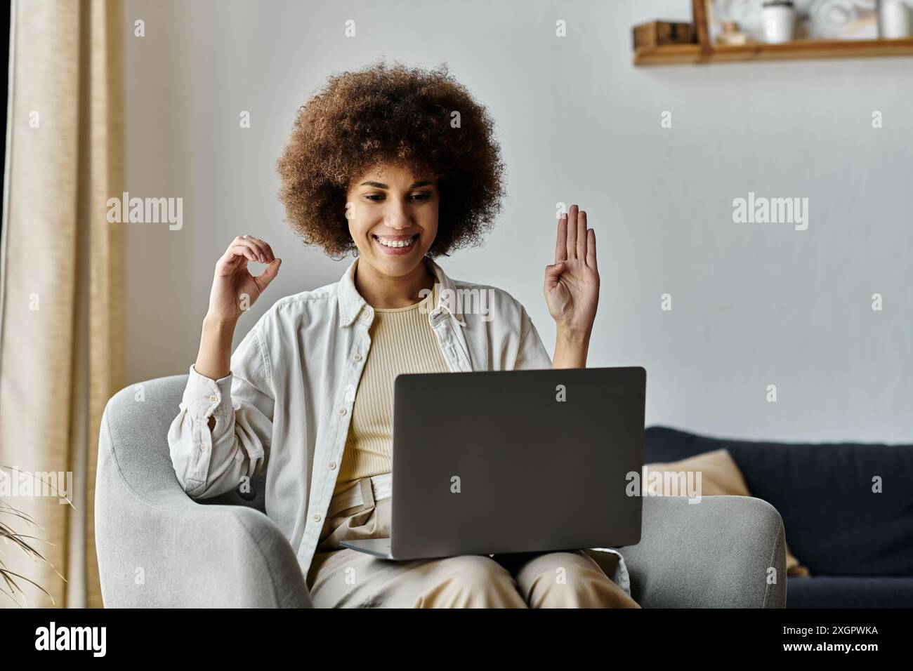 A woman sitting on a couch, using sign language while on a video call ...