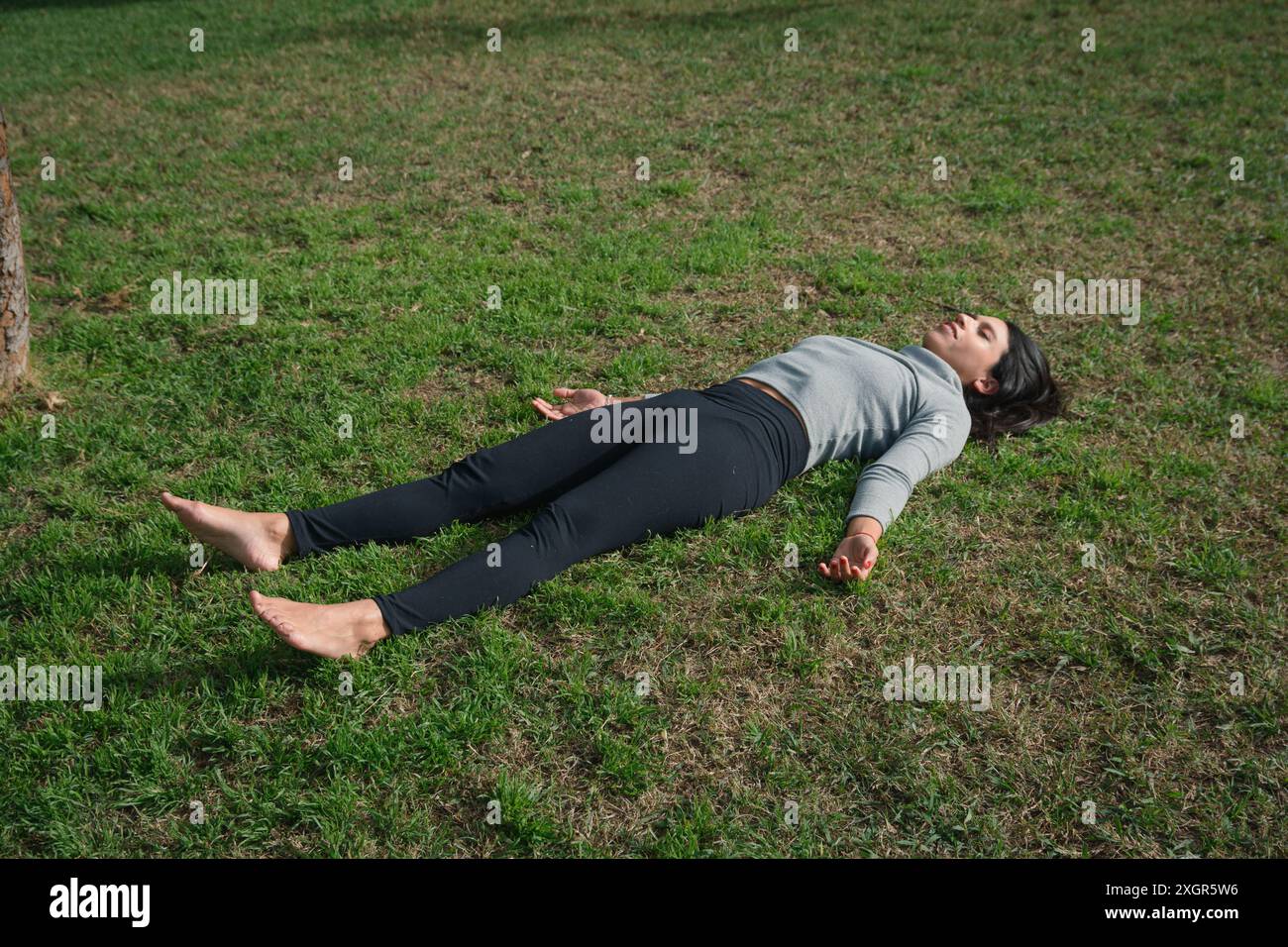 young latin woman lying on her back on grass with her arms and legs ...