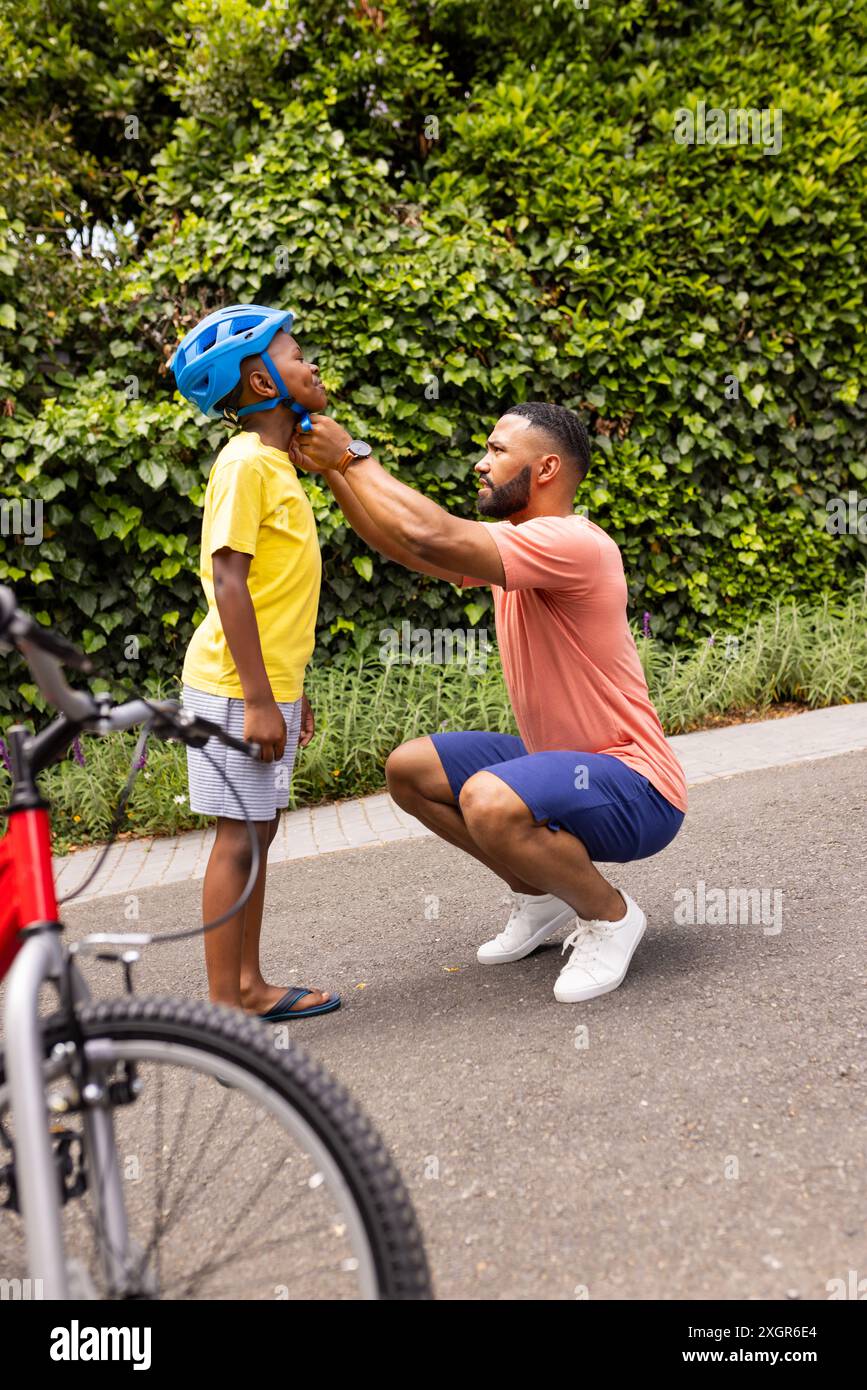 Young biracial father adjusts an African American son's helmet outdoors ...