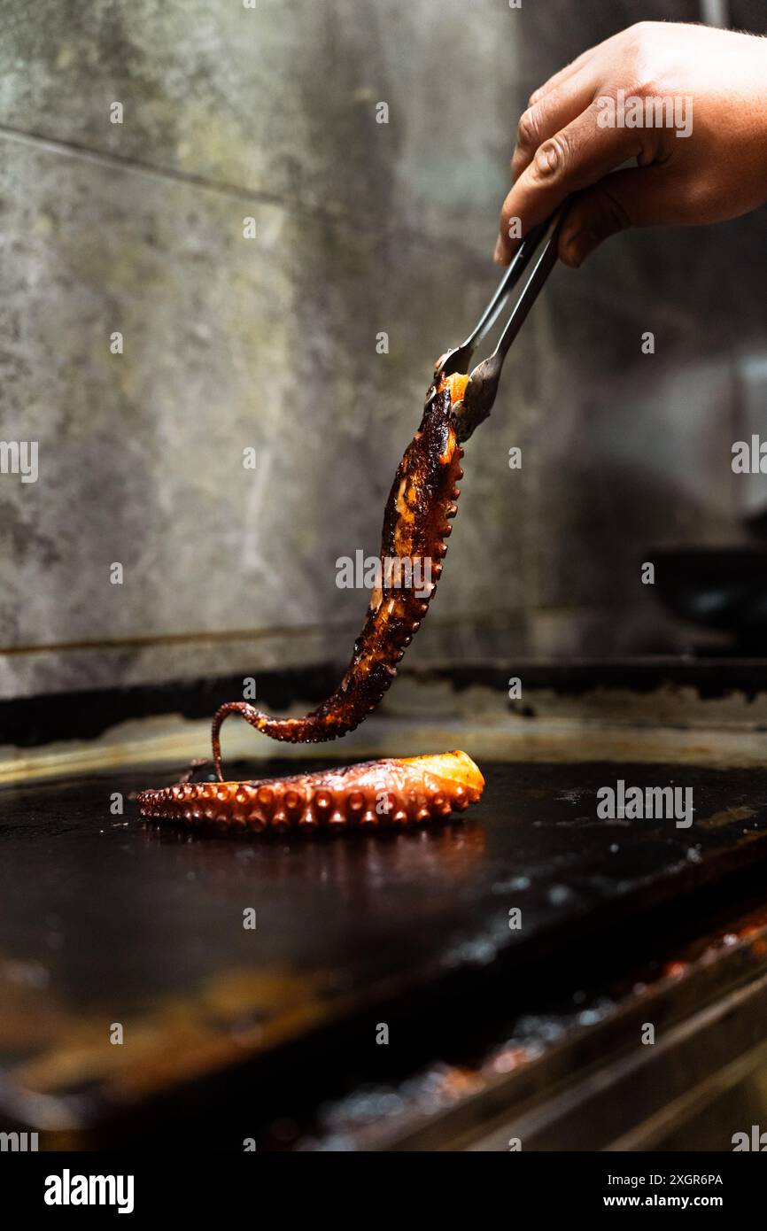 Hand of a cook catching an octopus tentacle with the tongs on a ...