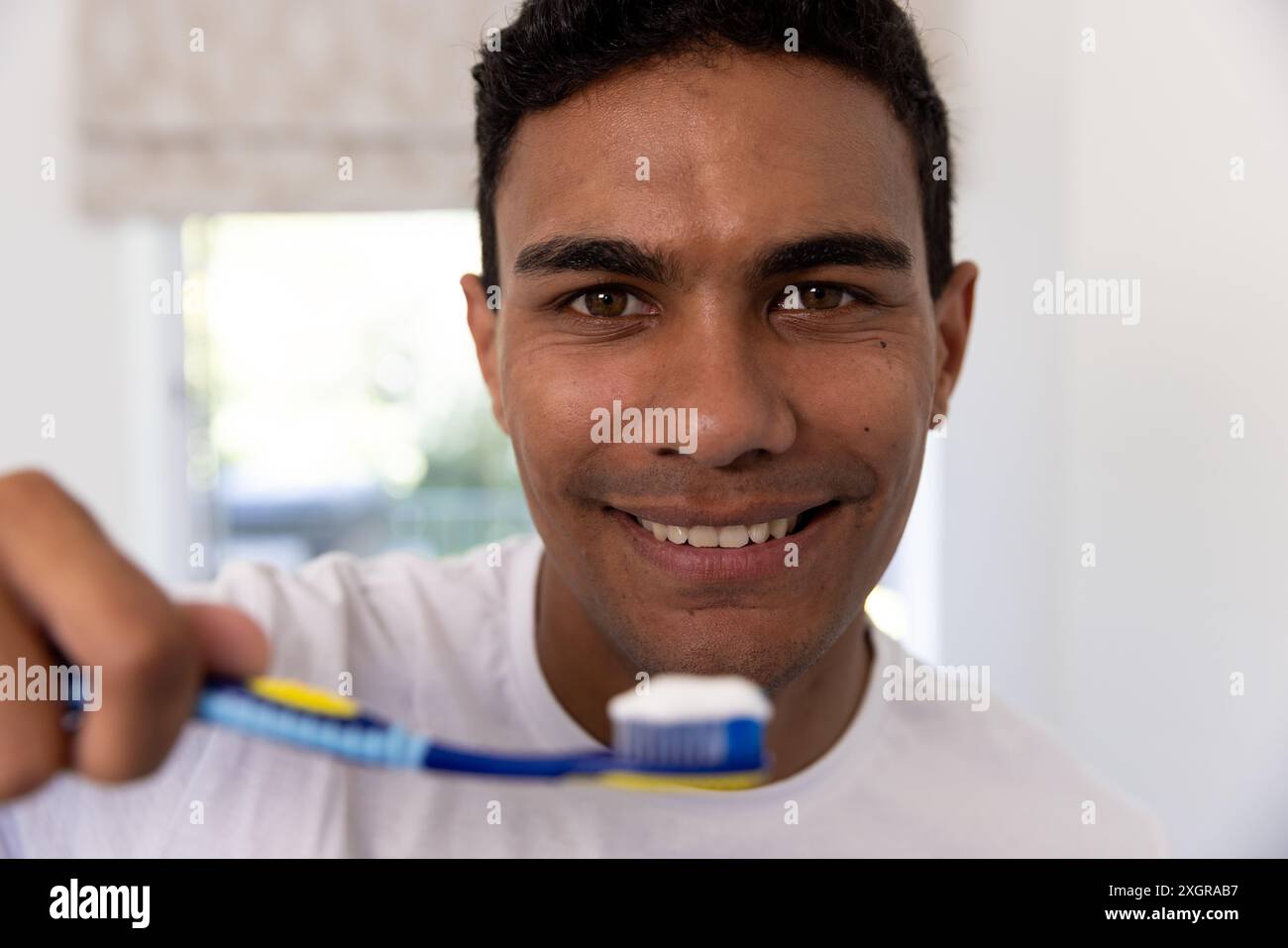 Young biracial man brushing teeth at home, with copy space. He promotes ...