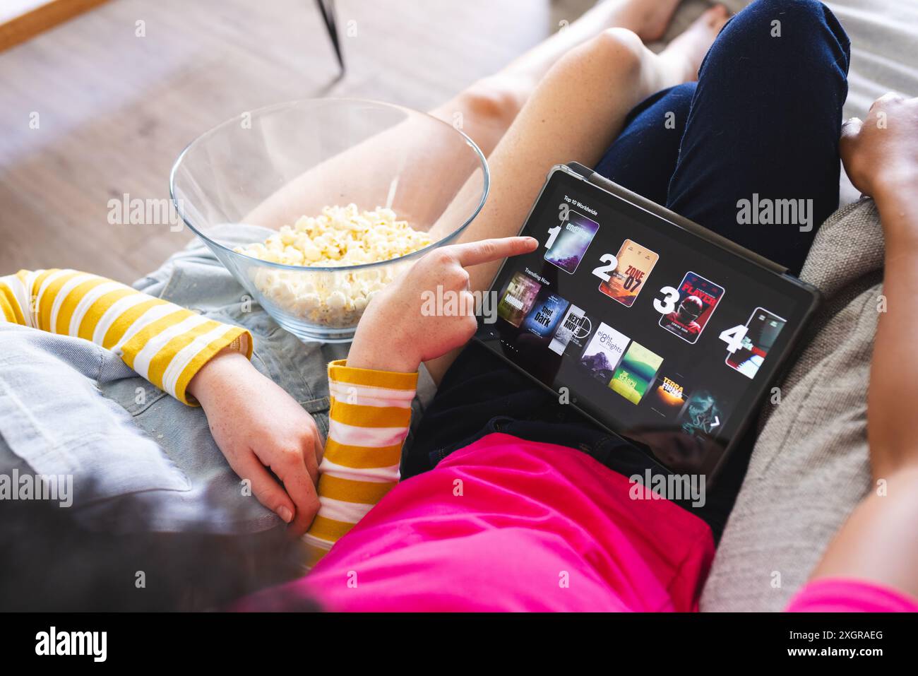 Diverse female friends on couch watching movie on tablet and eating ...