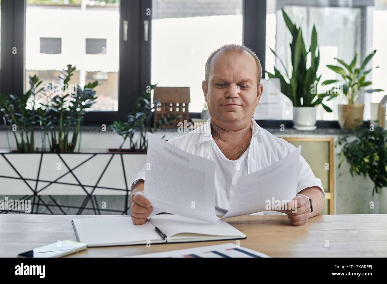 A man with inclusivity sits at a desk in an office reviewing paperwork ...