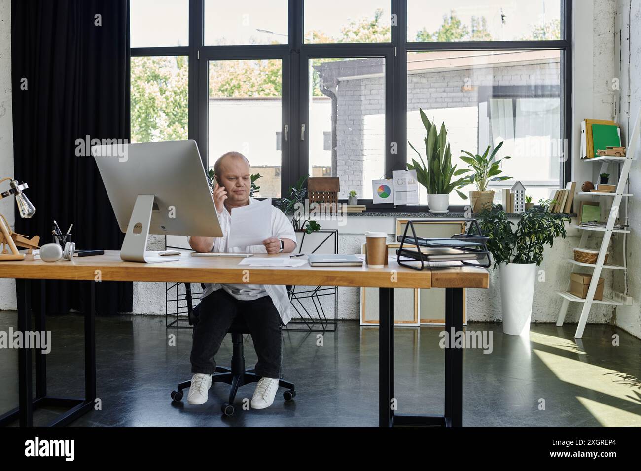 A man with inclusivity sits at his desk in an office, working on his ...