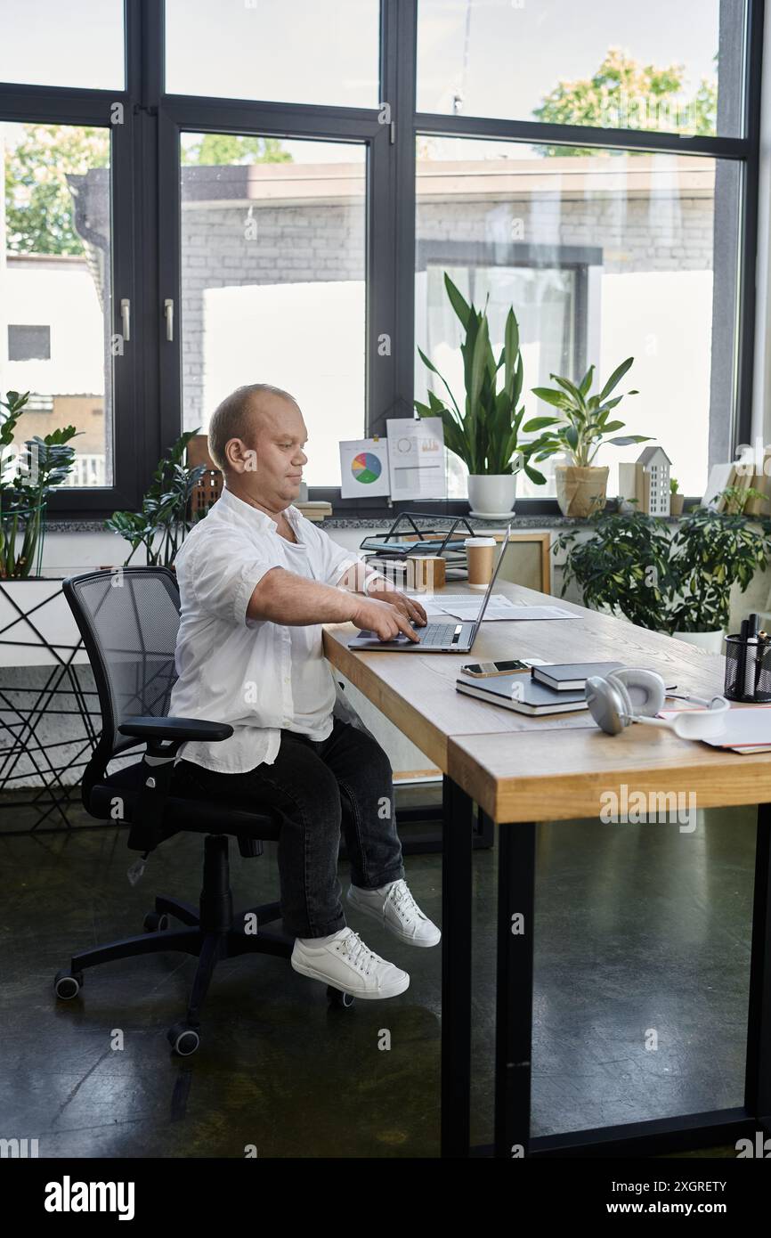 A man with inclusivity sits at a desk in a modern office with large ...