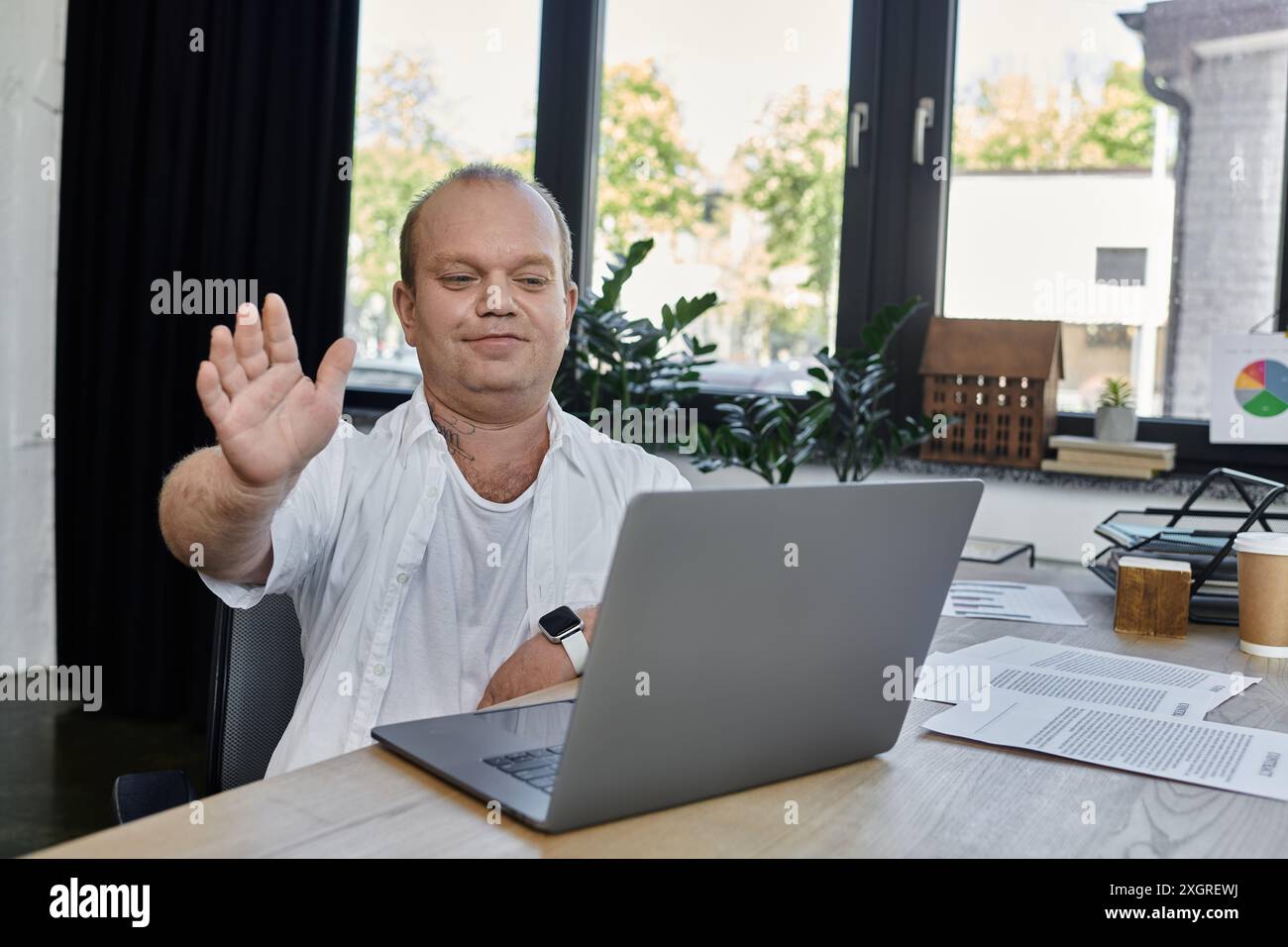 A man with inclusivity sits at a desk in an office, waving to the ...