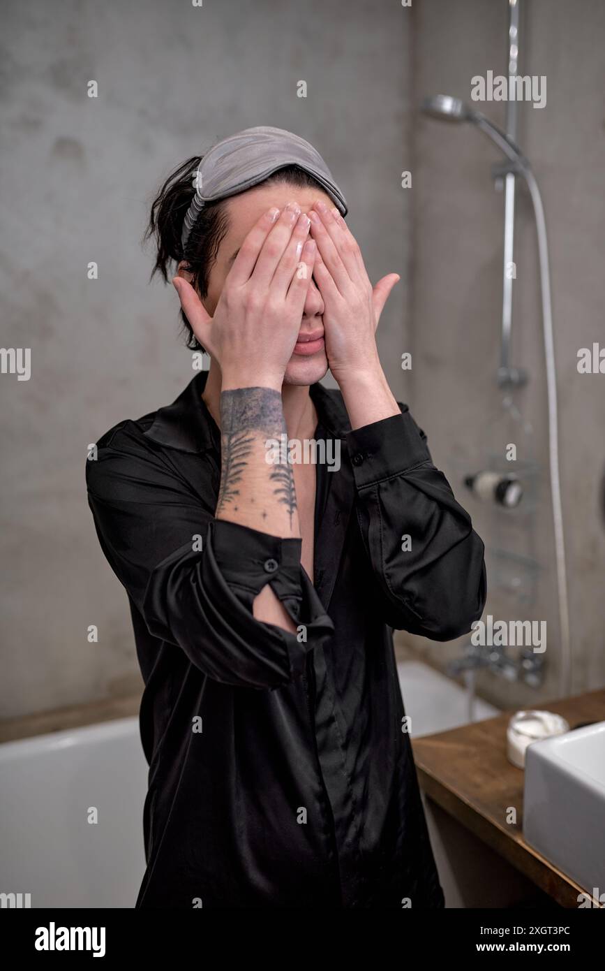 young gay with eyemask on his head wiping his eyes , washing face in ...