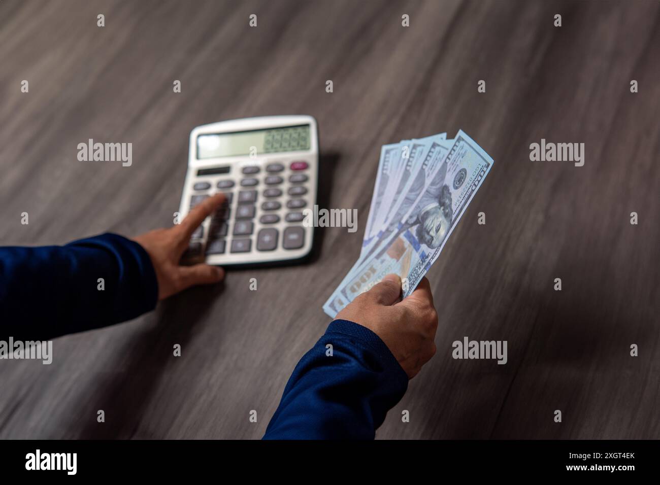 Close-up photo of a person's hands using a calculator and holding a wad ...