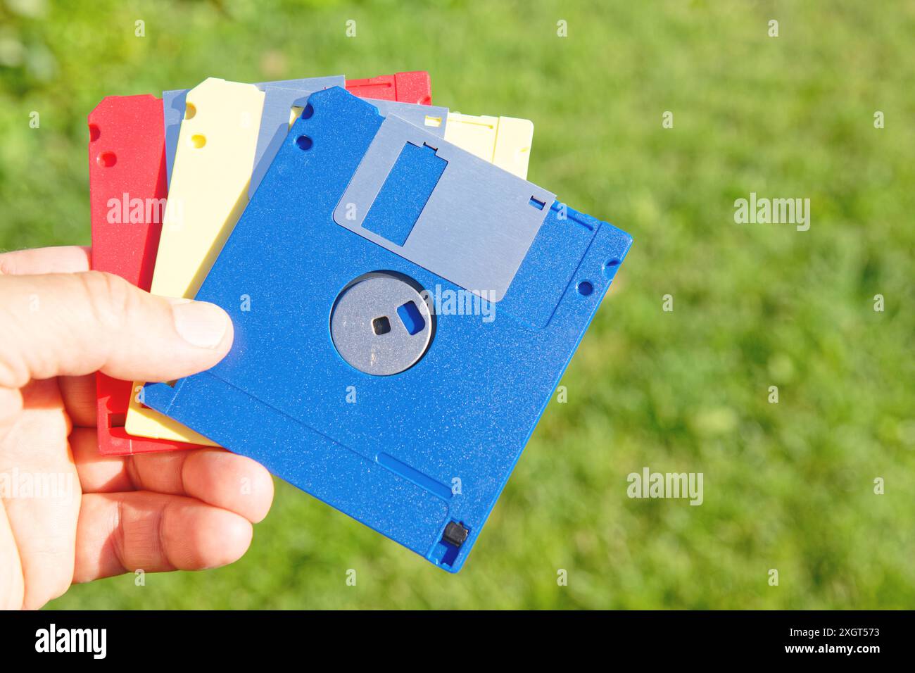 Vintage colored floppy disks in a hand on green grass lawn background ...