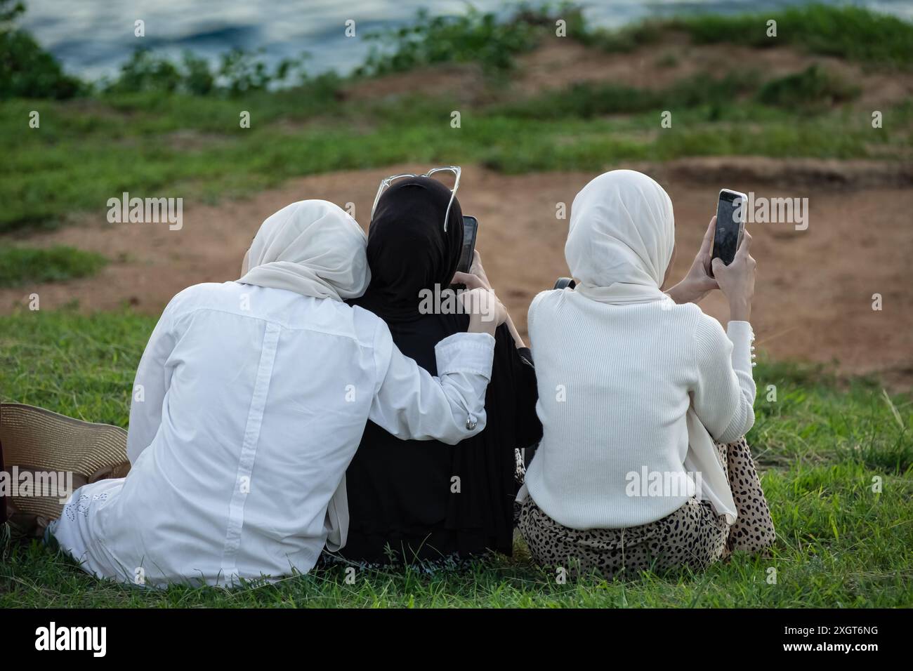 Back view of the muslim women relaxing on green grass in the nature ...