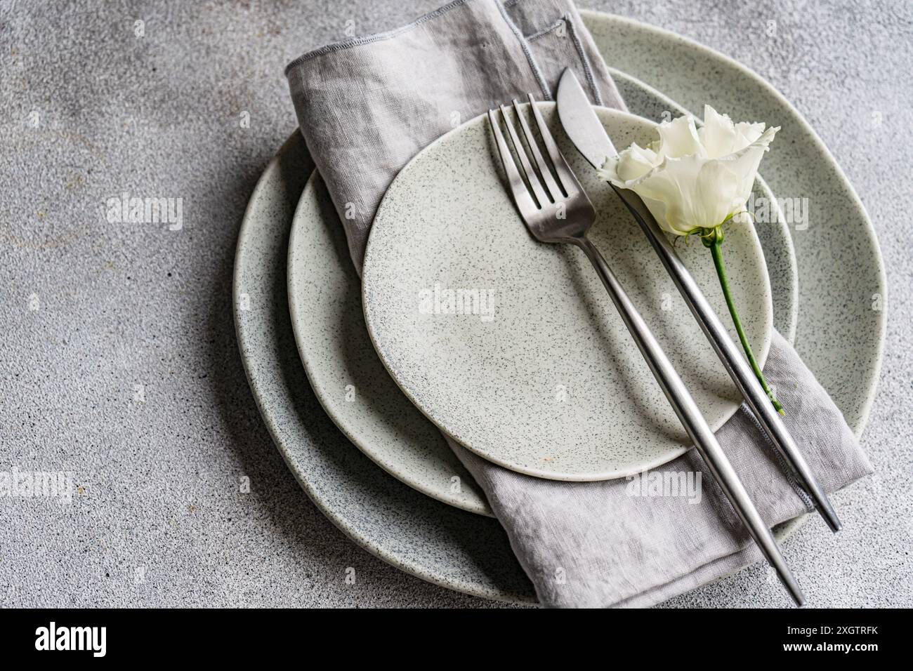 An elegant table setting featuring a stack of speckled ceramic plates ...
