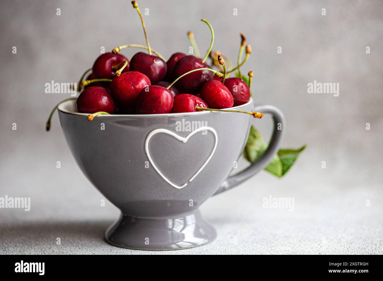 Ripe red cherries in a modern grey bowl with a heart-shaped cutout ...