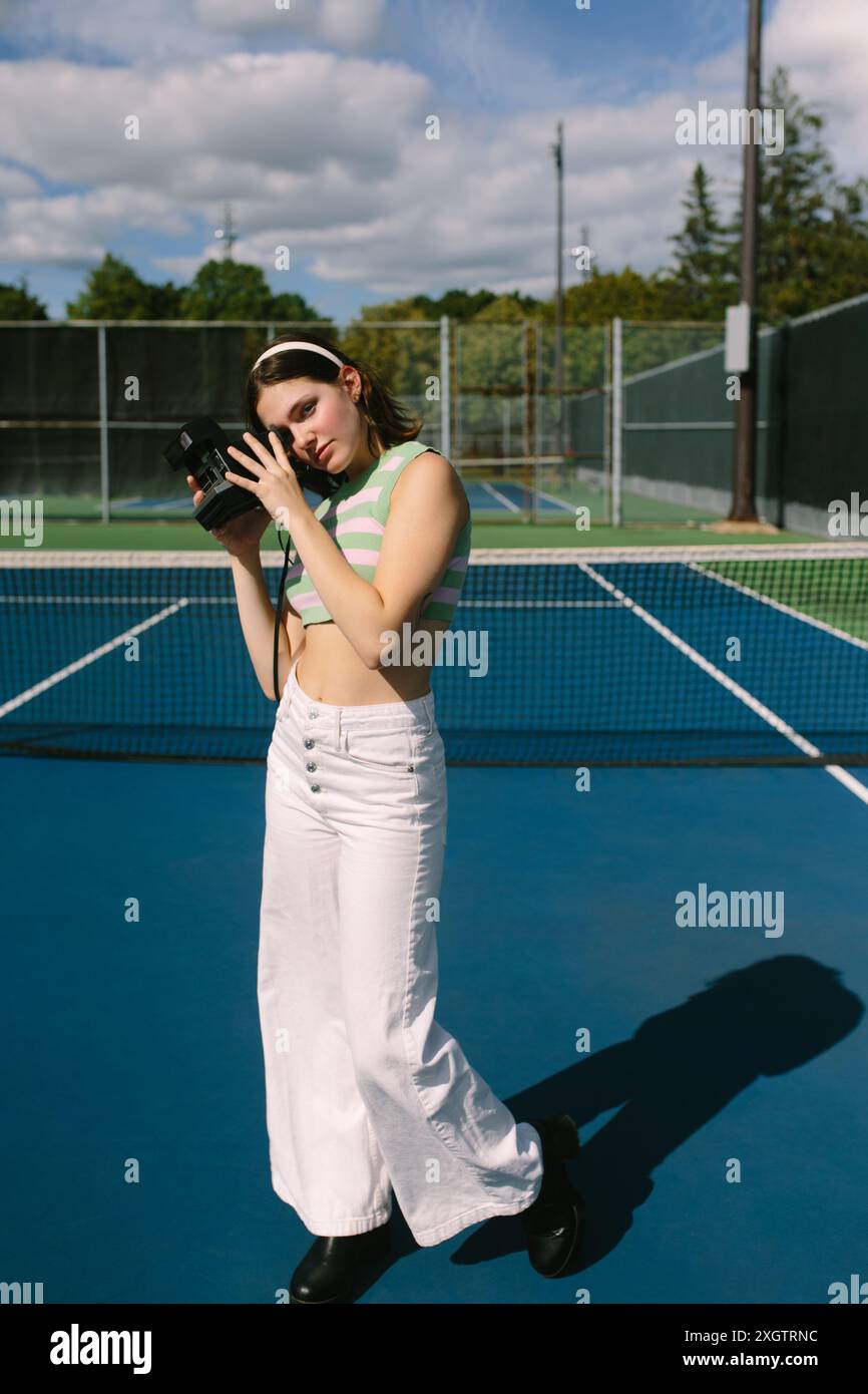 A stylish woman in a pastel-striped crop top and white pants poses with ... A stylish woman in a pastel-striped crop top and white pants poses with ...
