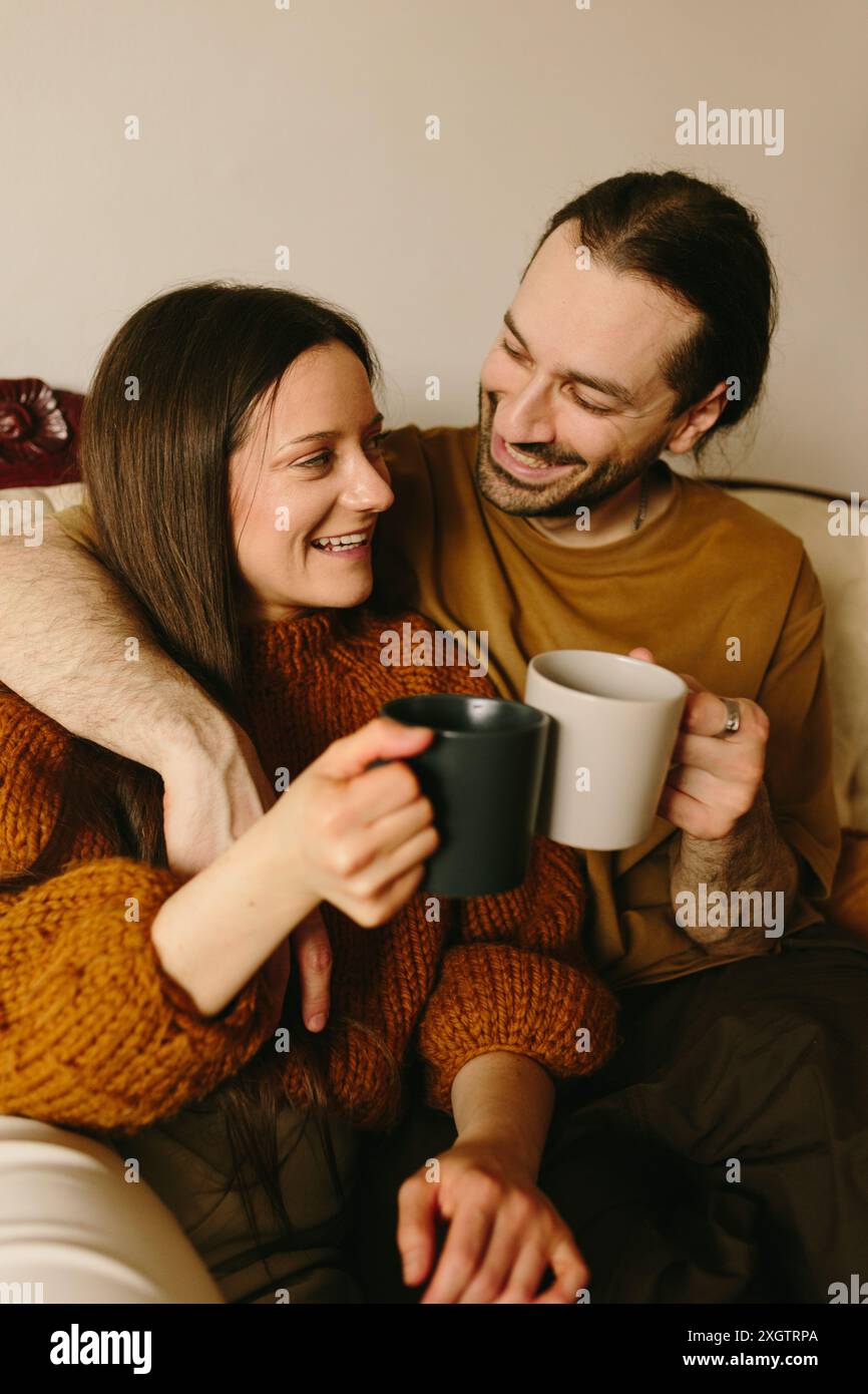 A Caucasian woman and man sitting closely on a cream-colored sofa ...