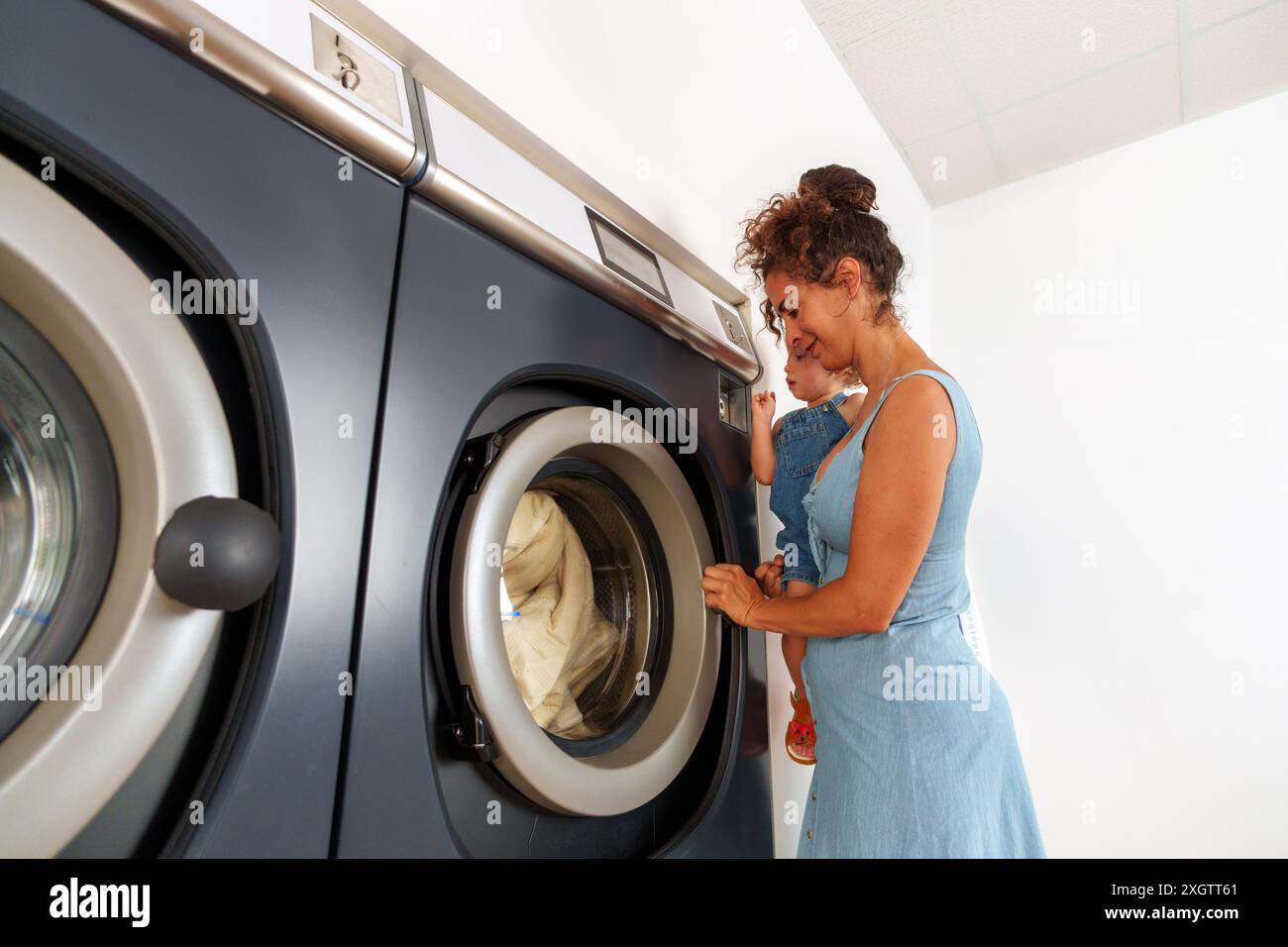 Hispanic woman loading washing machine with the help of her young son ...