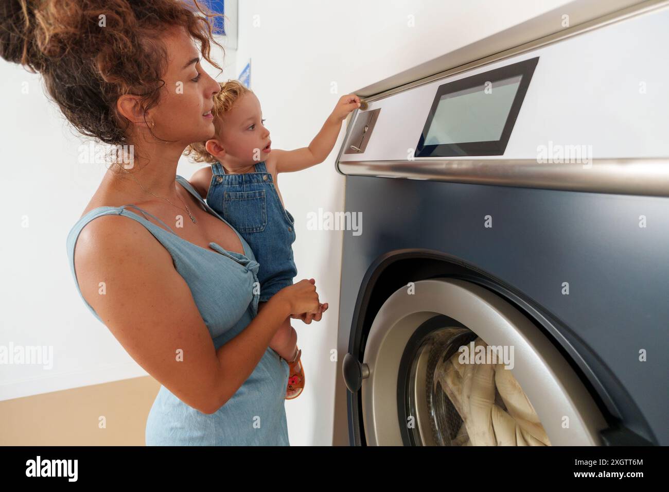 Toddler inserting a coin into the slot of the washing machine. Hispanic ...