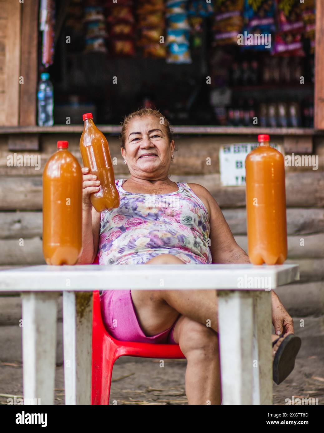 A happy Colombian woman sits at a market stall, holding bottles of ...