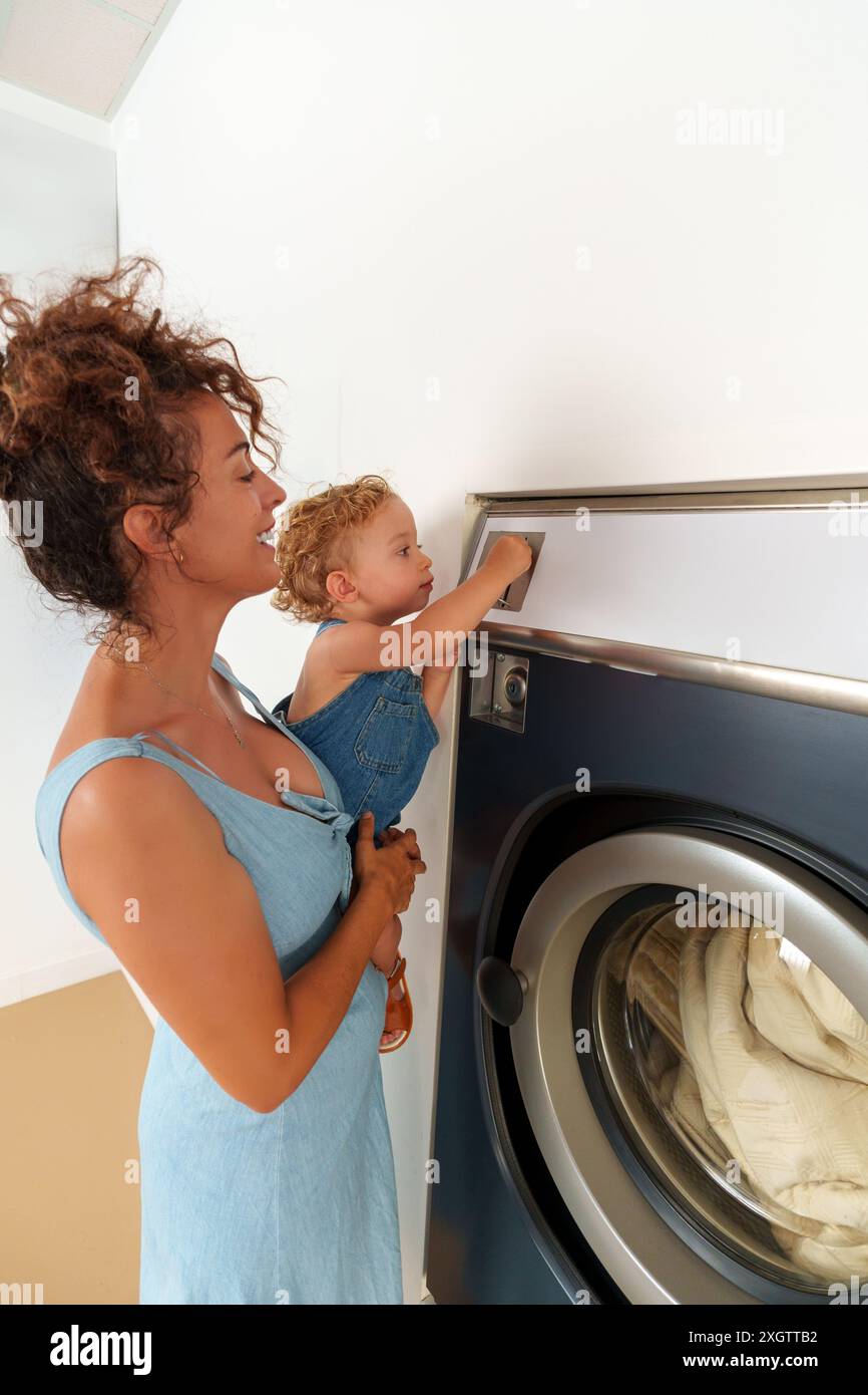 Toddler inserting a coin into the slot of the washing machine. Hispanic ...