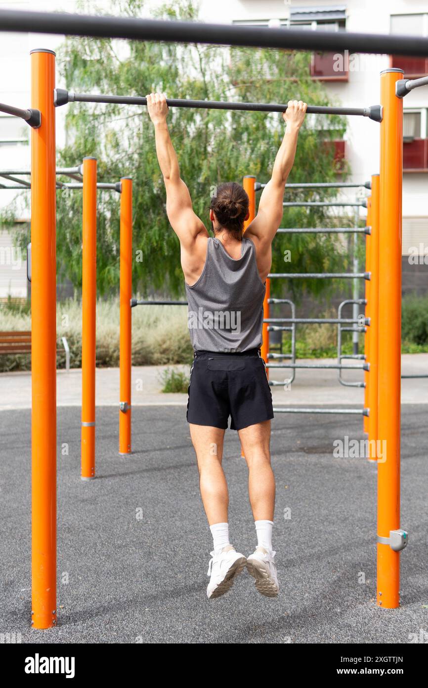 Anonymous athletic young man performing pull-ups at a vibrant orange ...