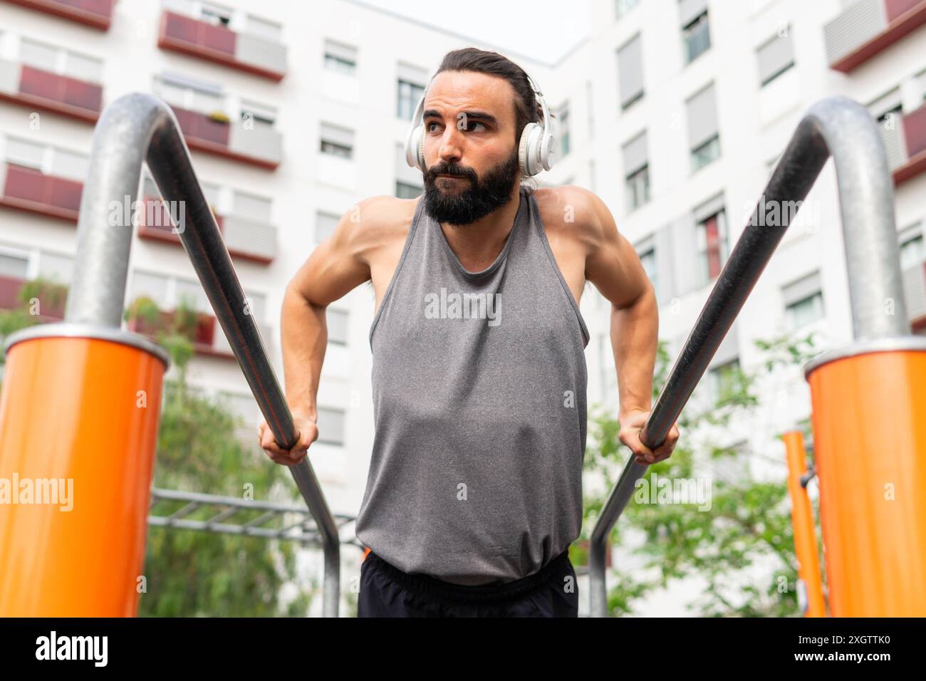 A focused man with a beard uses parallel bars at an outdoor gym against ...