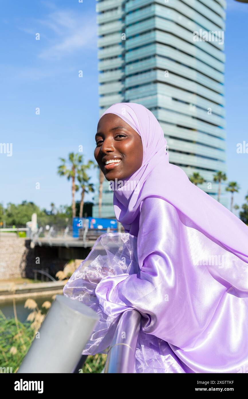 A woman, clad in a bright purple hijab and garments, laughs joyfully ...
