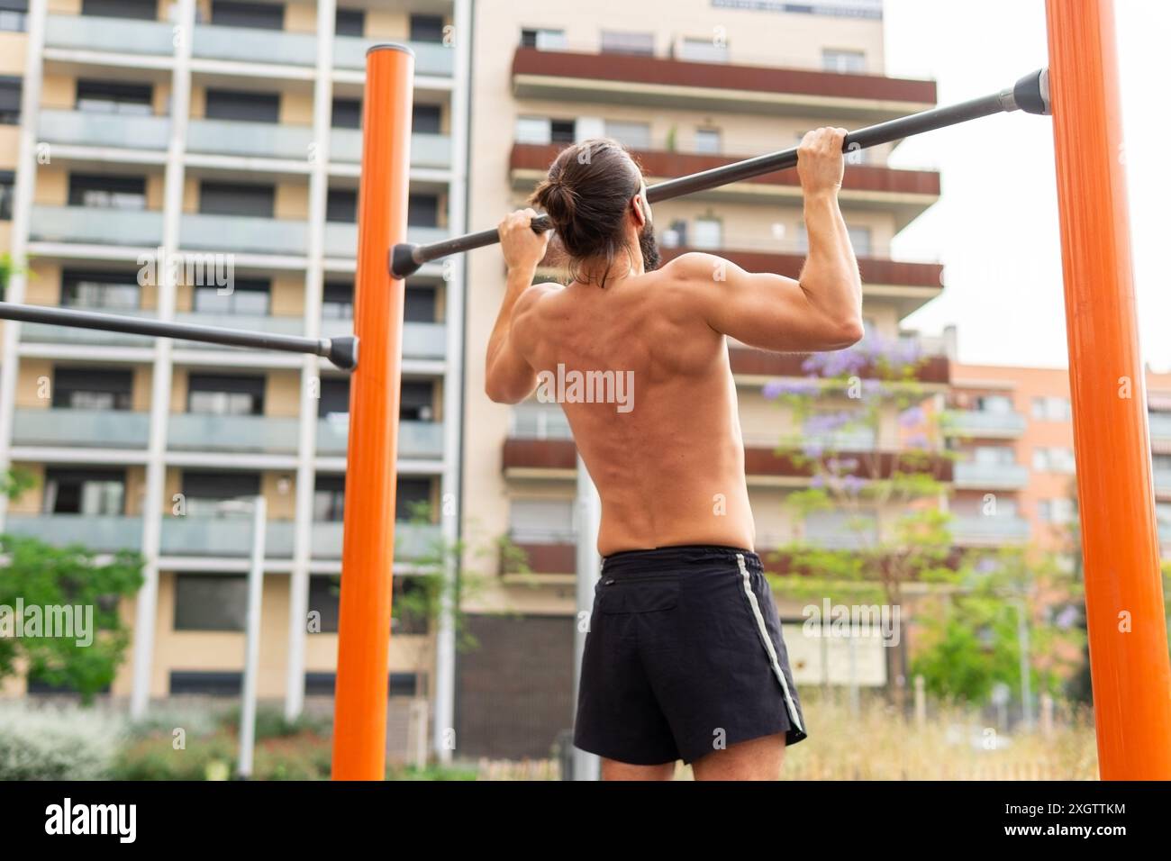 Anonymous muscular man in shorts performs pull-ups on an orange bar at ...