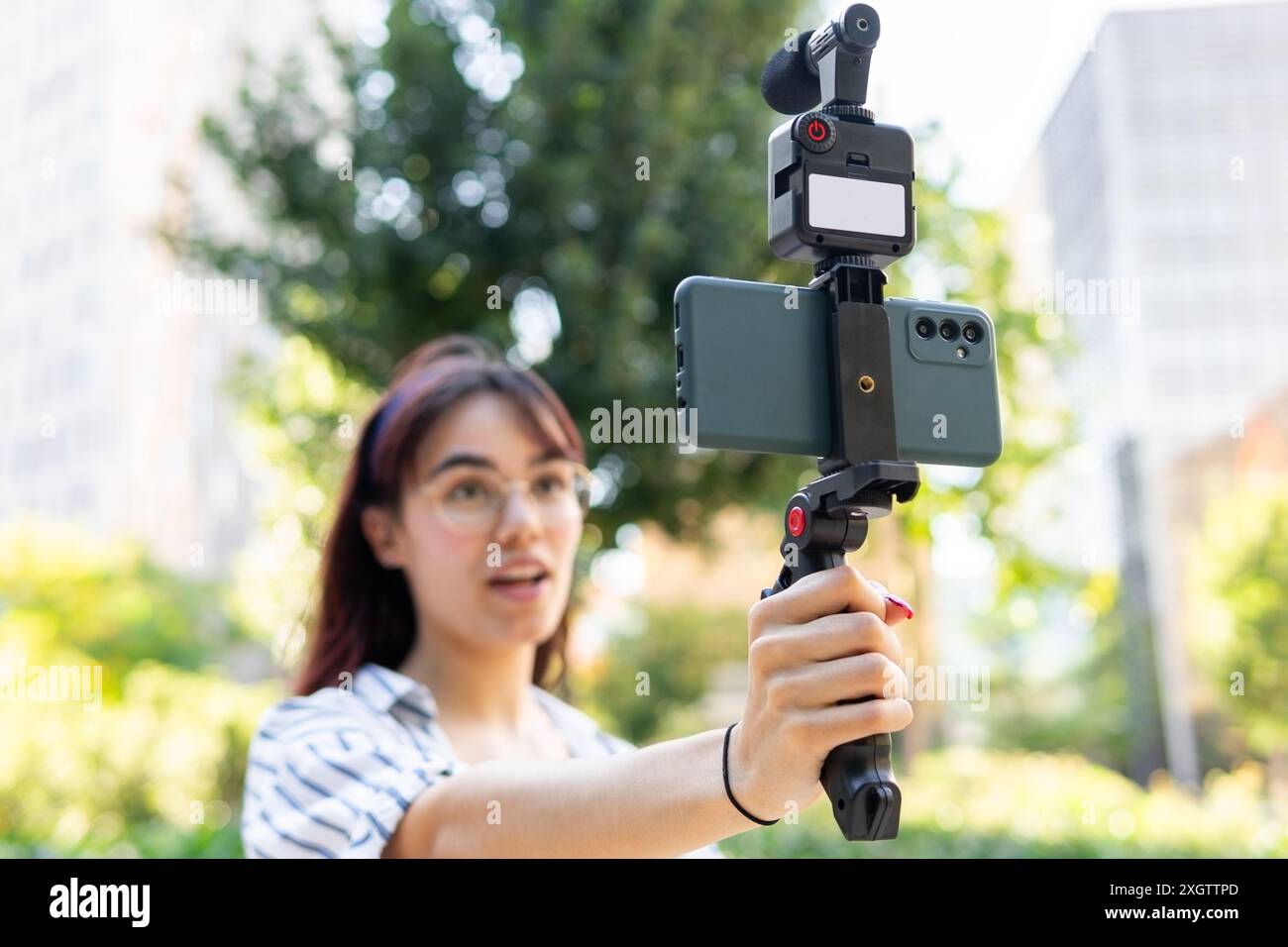 A young woman captures video using a smartphone stabilizer in a sunny ...