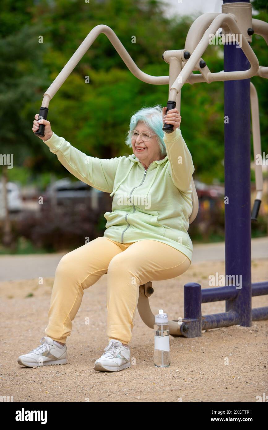 A cheerful elderly woman engages in physical exercise using outdoor gym ...