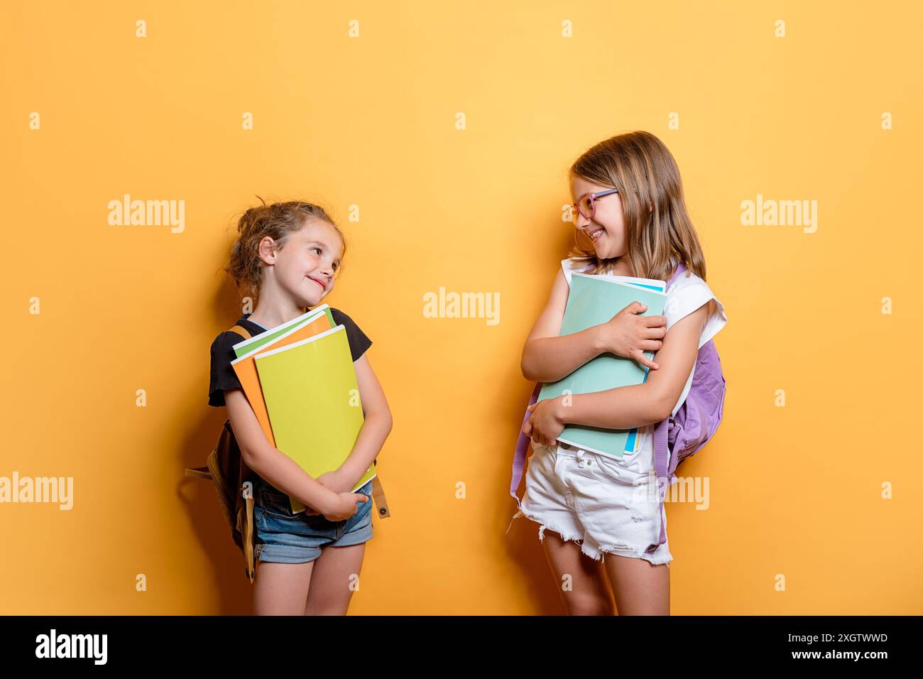 Two young girls, each holding school books, share a joyful moment in a ...