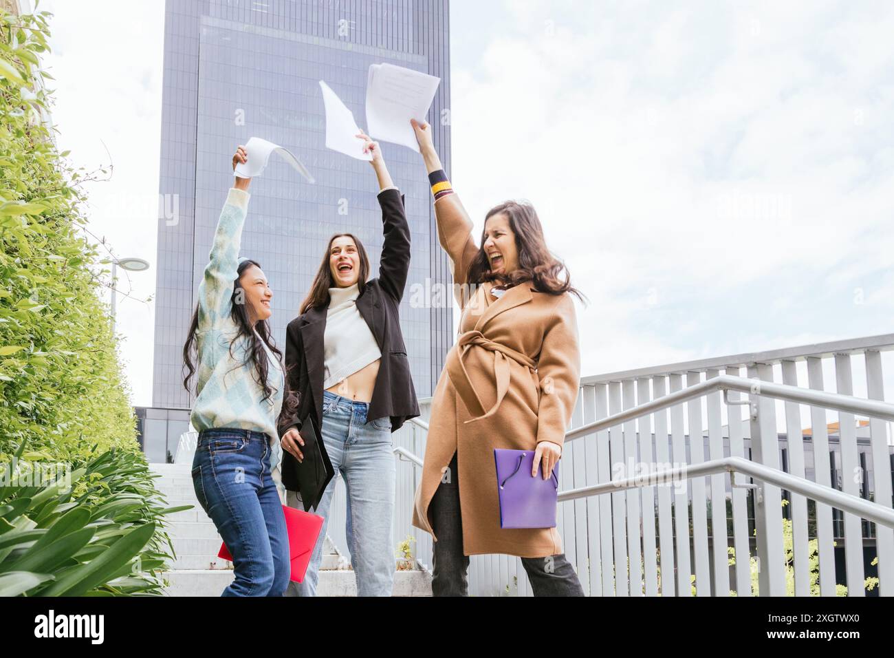 Three young female students joyfully celebrating with papers in hand ...