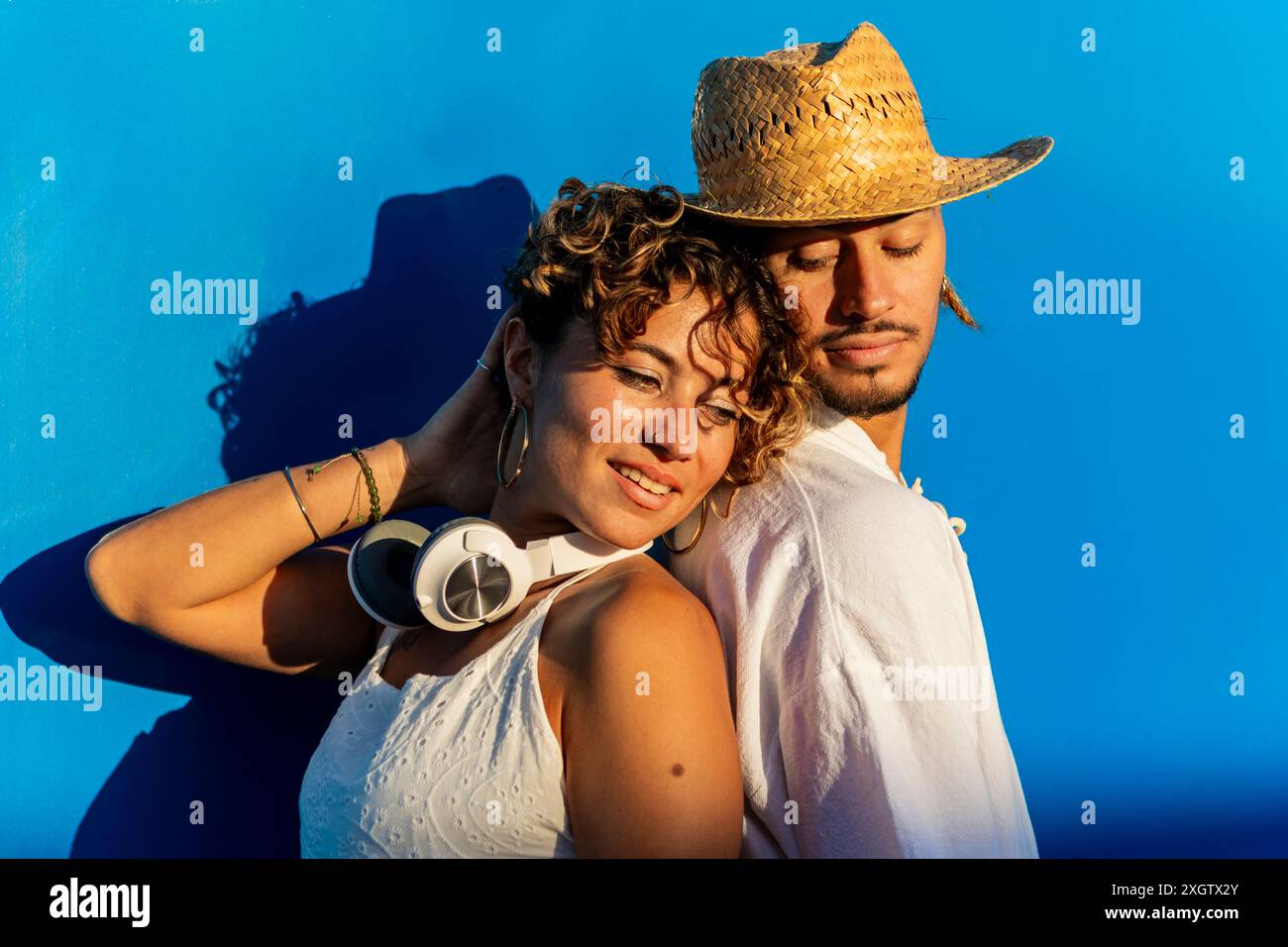 A Caucasian woman and man closely embrace against a vivid blue backdrop ...