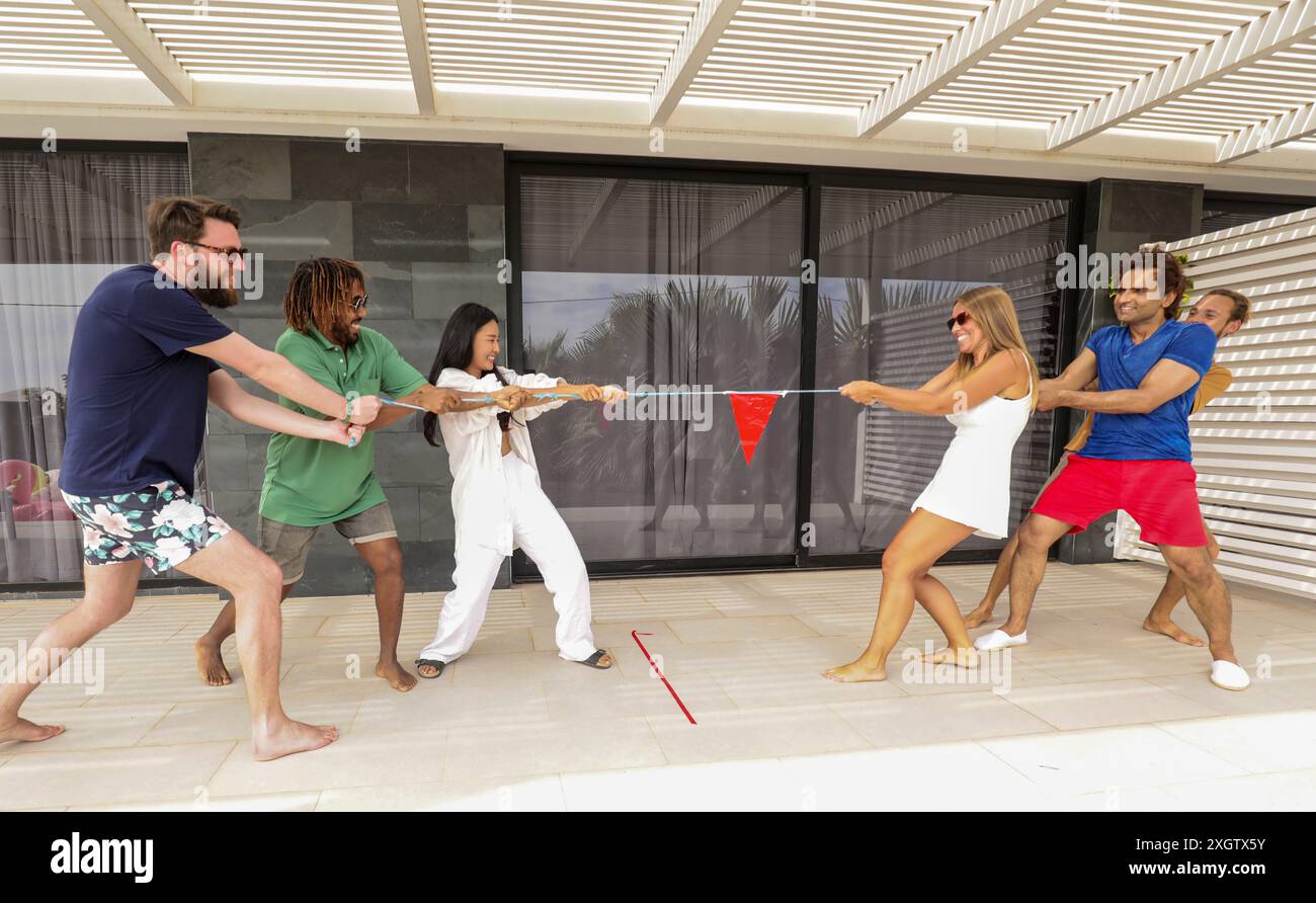 A diverse group of six friends engage in a tug-of-war game at a ...
