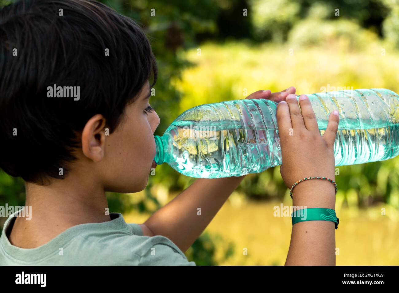 Side view of a boy quenches his thirst by drinking water from a large ...