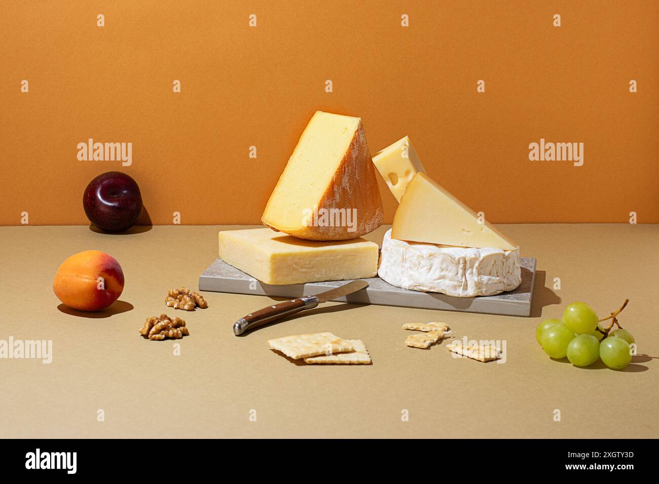 Top view of assorted cheeses alongside fruits and nuts on a neutral ...