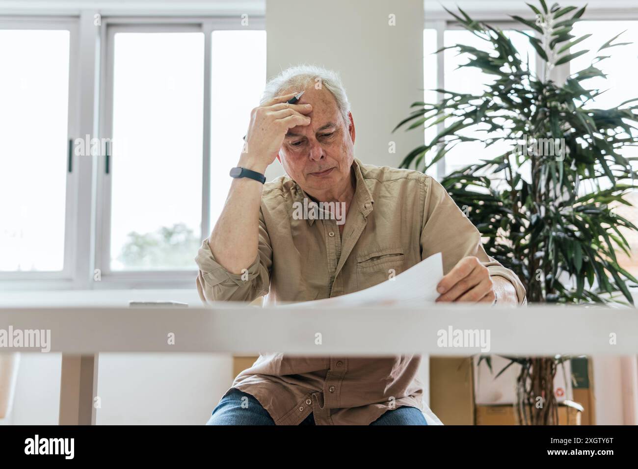 A thoughtful elderly Caucasian man reviews documents intently at a ...