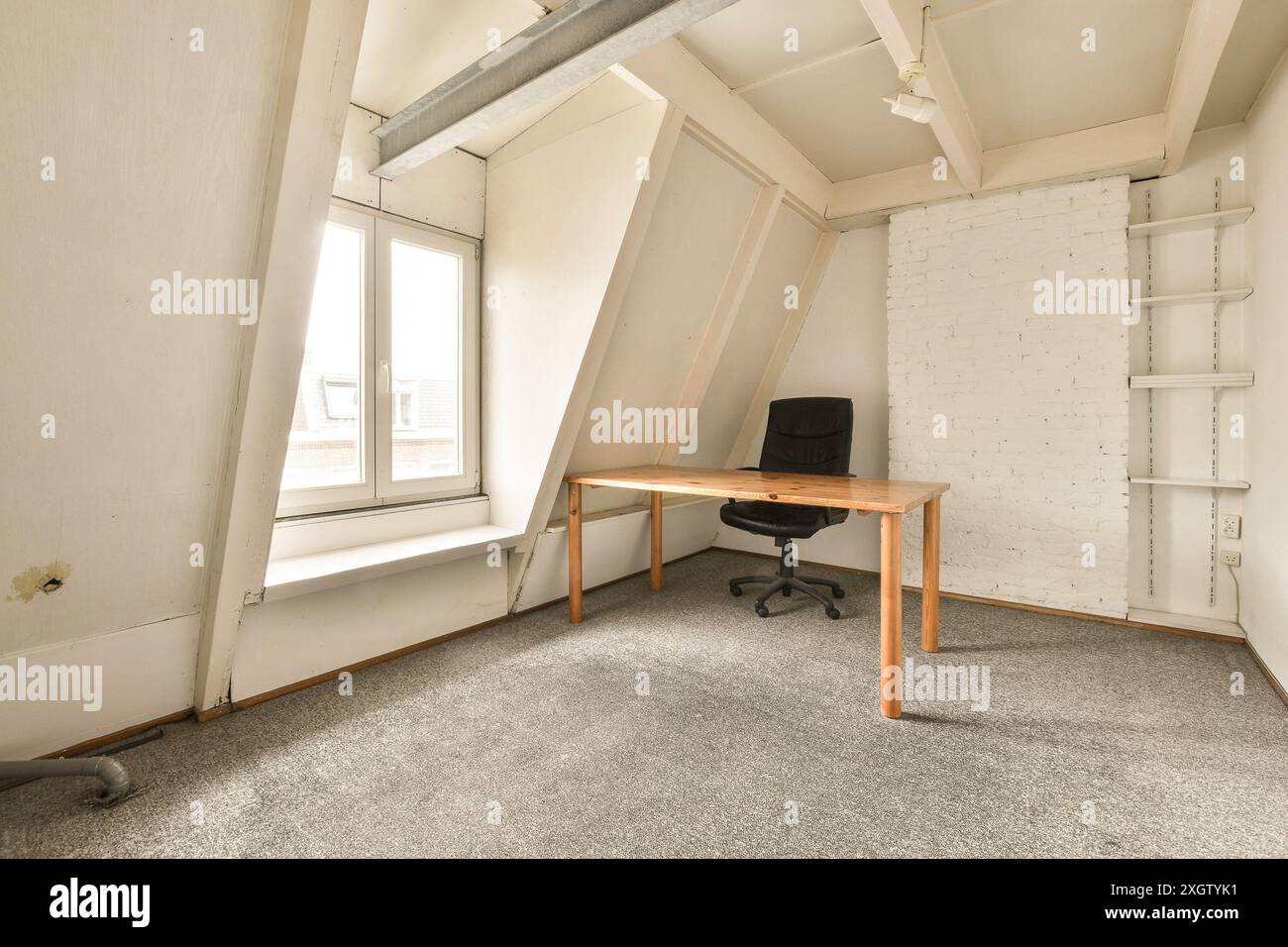 A bright, simple attic office with a wooden desk, black chair, and ...