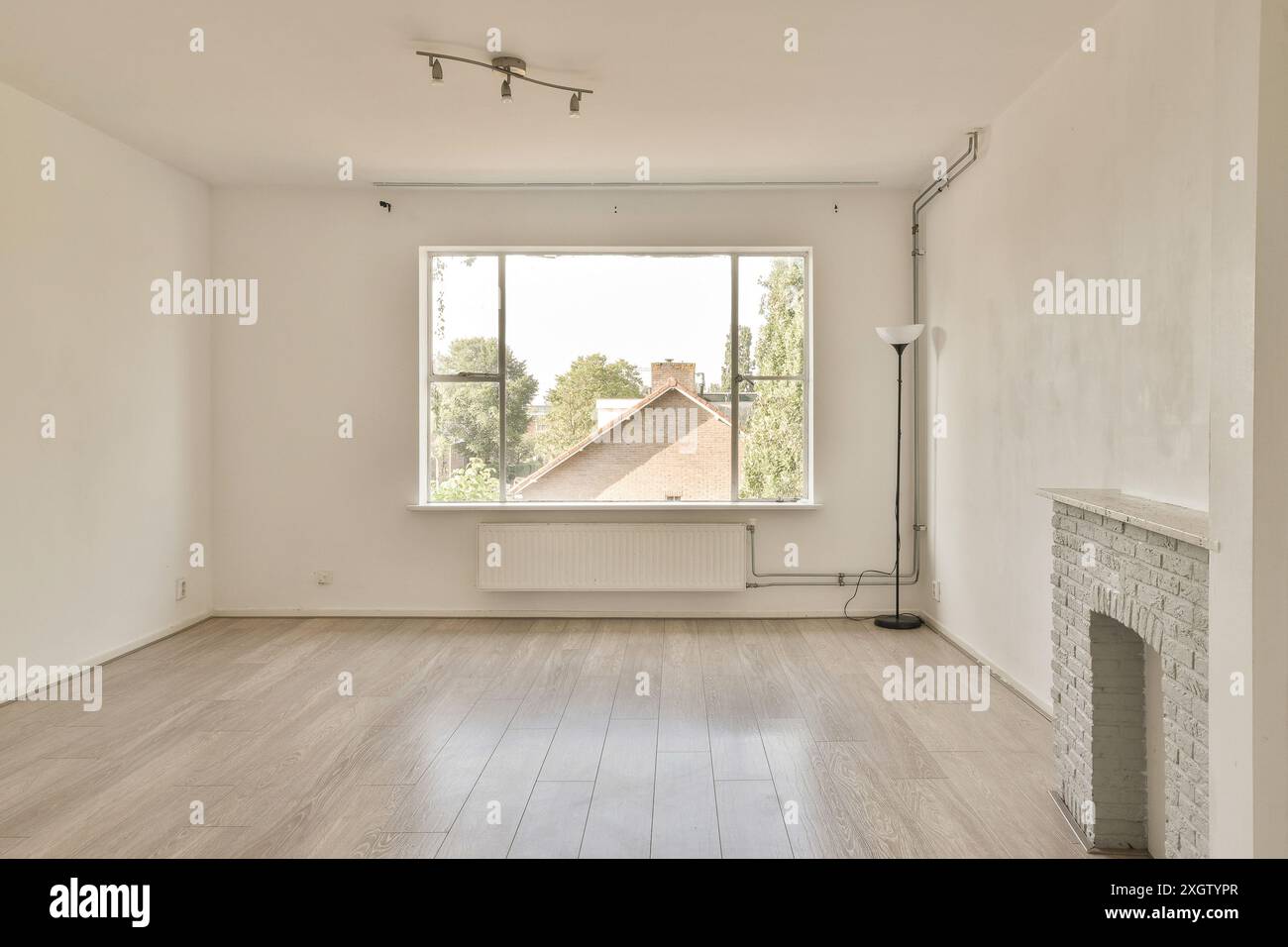 An empty, well-lit room with large windows, laminate flooring, and a ...
