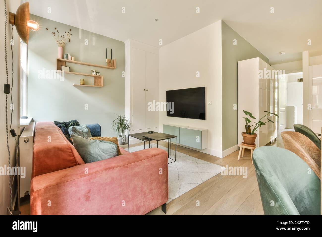 A spacious and well-lit living room featuring a coral sofa, green armchairs, and wooden accents ...