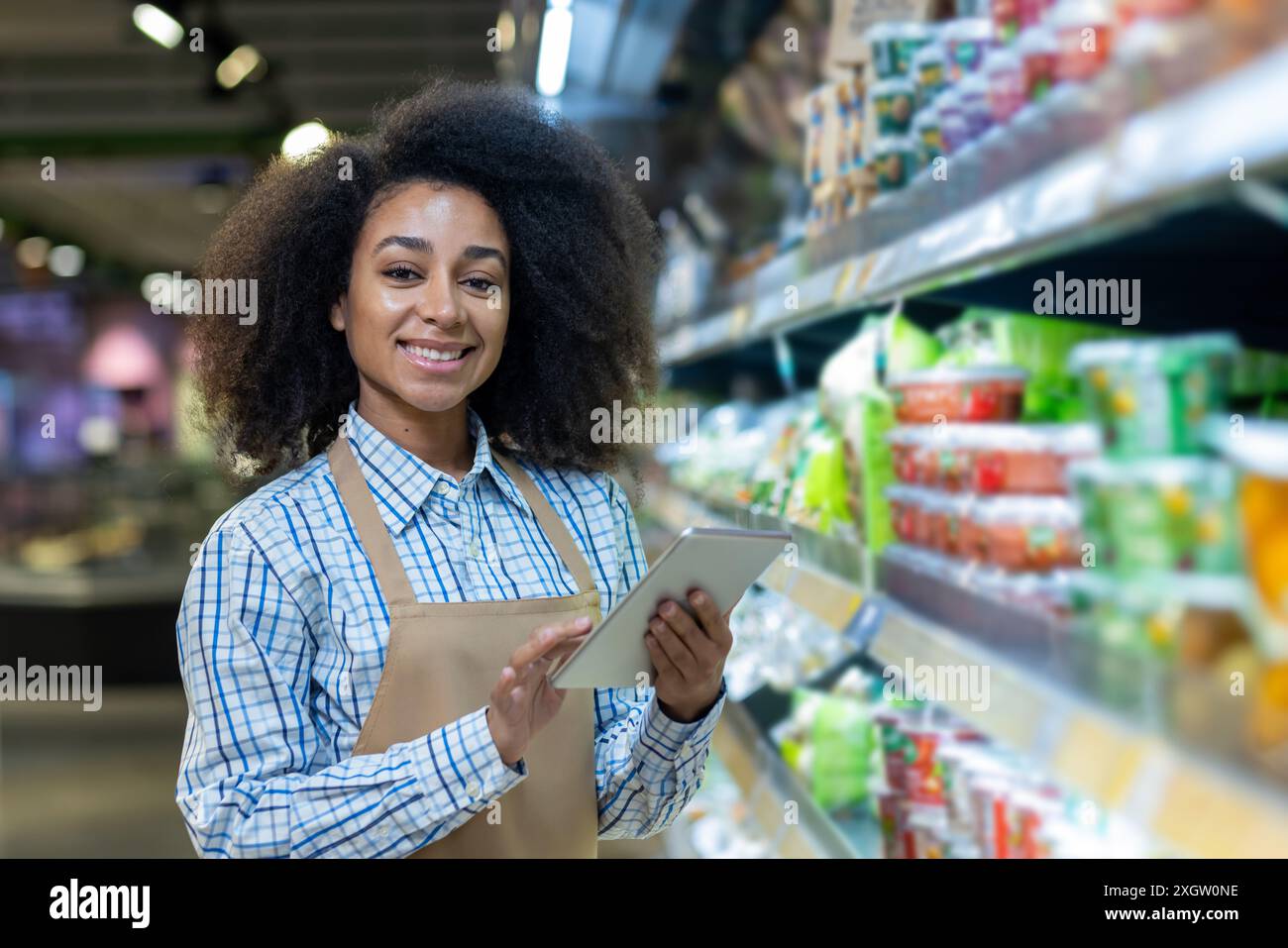 Confident supermarket employee using digital tablet while standing in ...