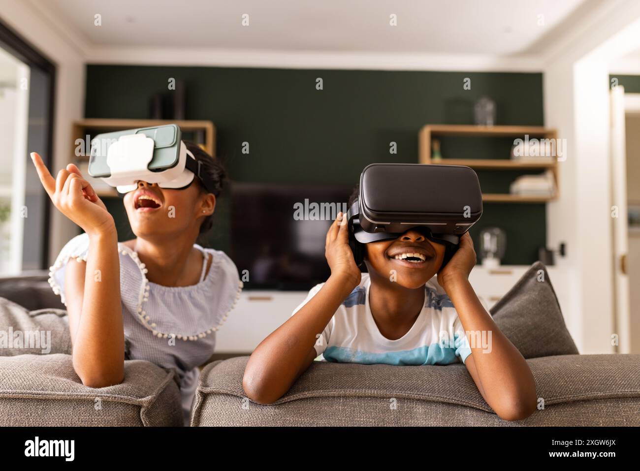 Teenage biracial brother and sister enjoy VR headsets at home. They're ...