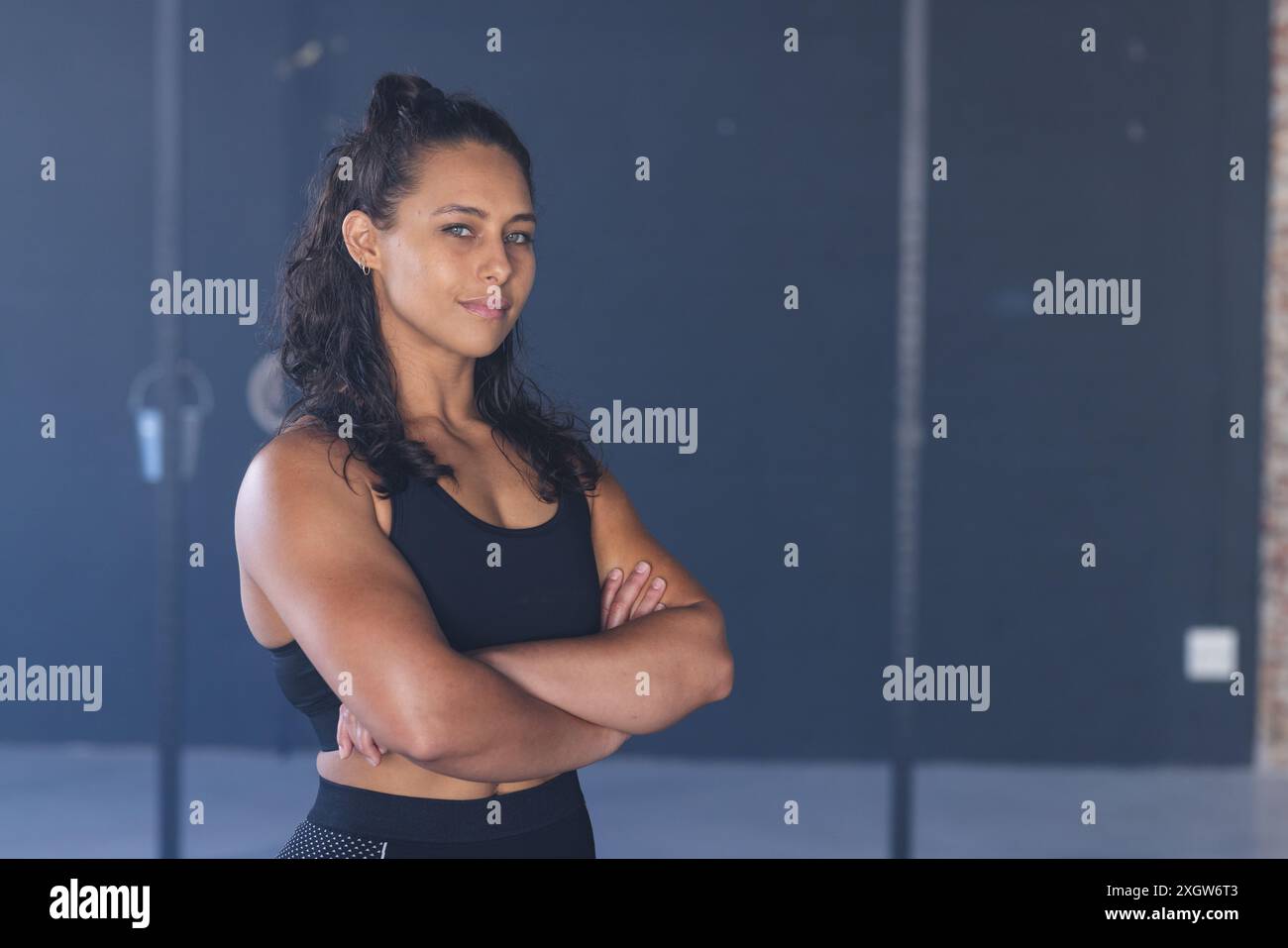A strong and fit young biracial woman stands confidently at the gym ...