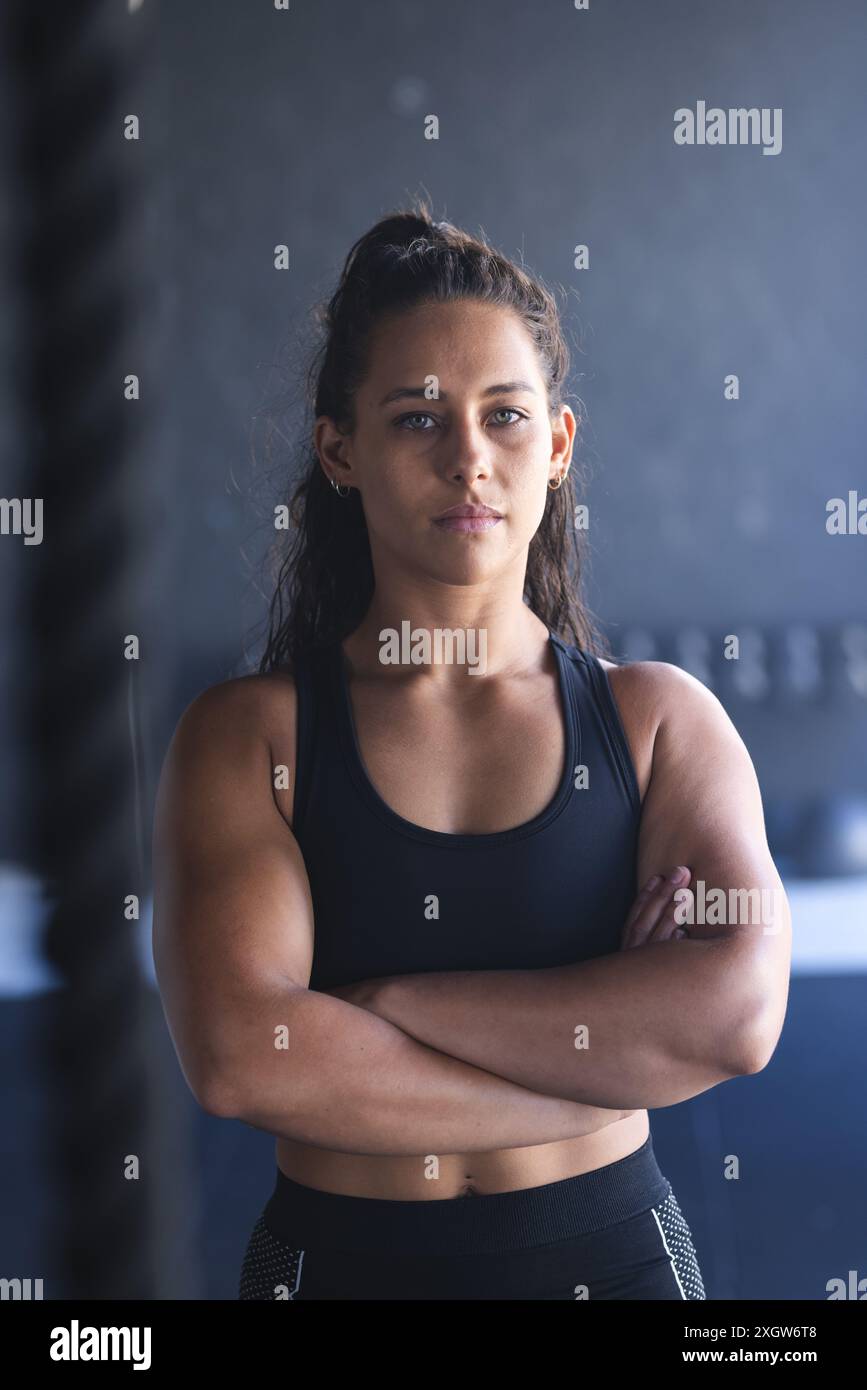 A strong and fit young biracial woman stands at the gym unaltered. Her ...