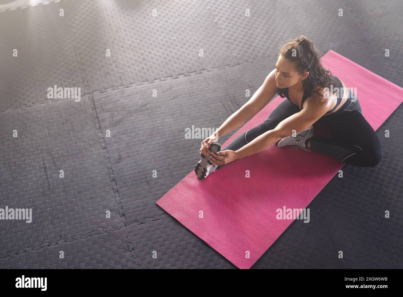 Strong and fit young biracial woman stretches on a pink mat at the gym ...