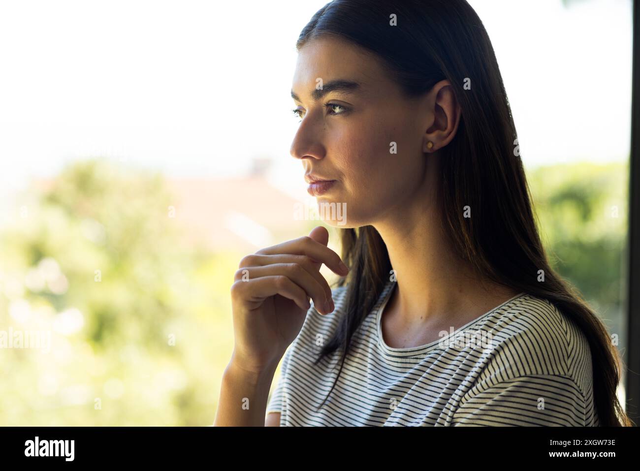 Teenage Caucasian girl looks thoughtfully out a window. Her pretty ...