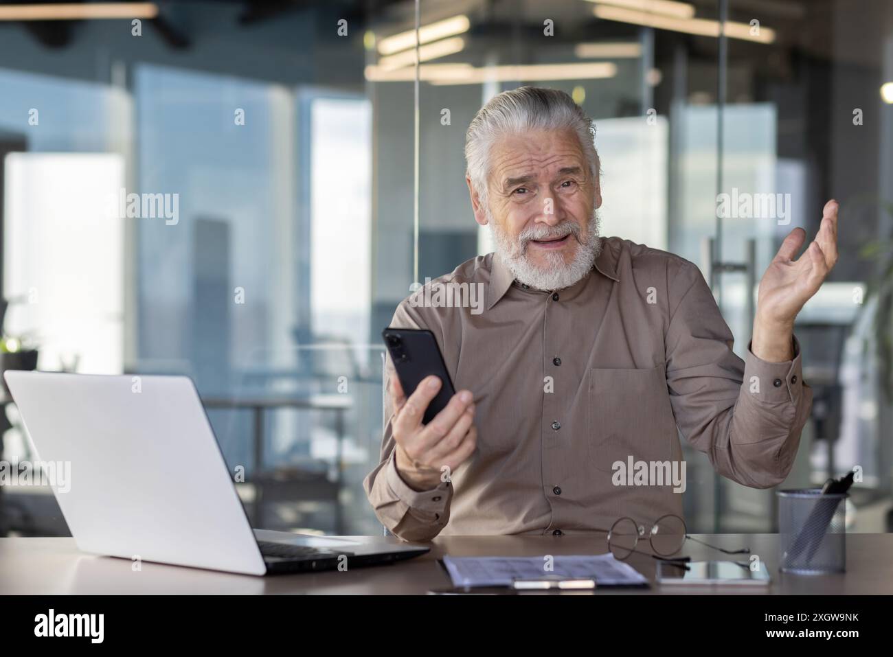 Elderly businessman expressing confusion while holding smartphone and ...