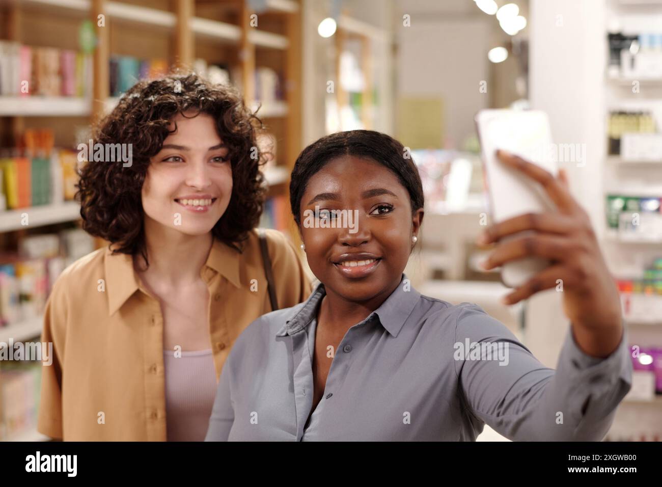 Two young smiling consumers taking picture on mobile phone while ...
