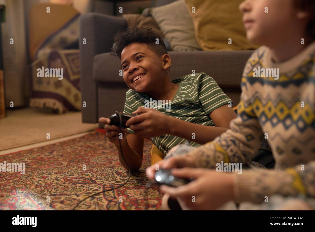 Medium shot of two diverse boys playing video games on carpeted floor ...